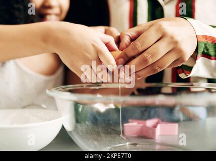 Backen, die Hände von Mutter und Mädchen mit Eiern brechen, während sie ...