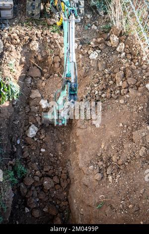 Minibagger gräbt einen Graben, um Rohre zu verlegen. Nahaufnahme eines ...