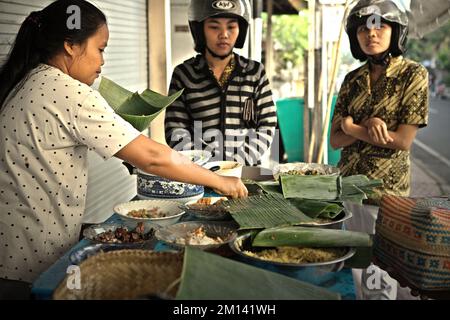 Eine Frau, die Kunden bei einem Straßenverkäufer bedient und Speisen ...
