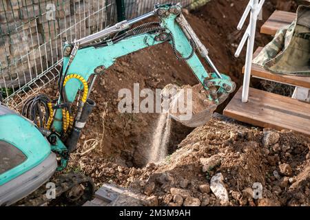 Minibagger gräbt einen Graben, um Rohre zu verlegen. Nahaufnahme eines ...