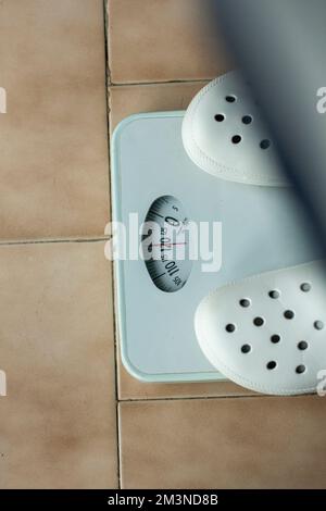 Analoge Waage, auf der eine Person gewogen wird und deren Gewicht in kg ...