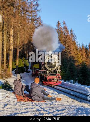 Ein paar Männer und Frauen beobachten die Dampfeisenbahn im Winter im ...