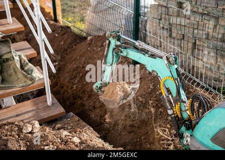Minibagger gräbt einen Graben, um Rohre zu verlegen. Nahaufnahme eines ...