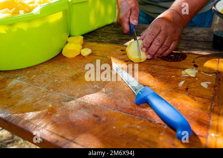 Ein älterer Bauernkocher schneidet Kartoffeln mit einem Messer in ...