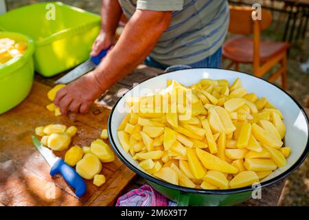 Ein älterer Bauernkocher schneidet Kartoffeln mit einem Messer in ...