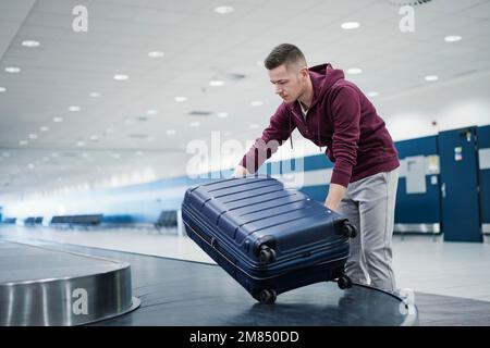 Reisen mit dem Flugzeug. Der Passagier holt seinen blauen Koffer in der ...