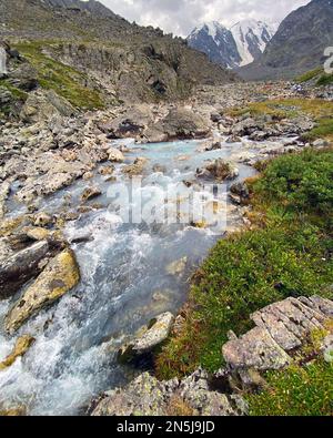 Der Alpenfluss fließt an einem hellen Tag über Steine aus den Bergen ...