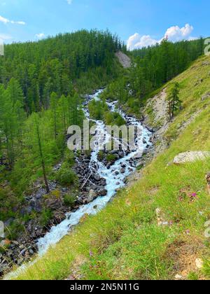 Der Alpenfluss fließt an einem hellen Tag über Steine aus den Bergen ...