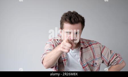 Der junge europäische Mann starrt bedrohlich in die Kamera und zeigt mit dem Zeigefinger, und ...