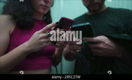 Ein Paar, das im Fahrstuhl auf seine Handys schaut. Mann und Frau sind abhängig von ihren Handys ...