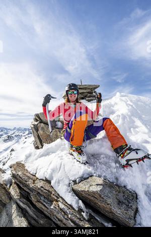 Glücklicher Bergsteiger mit Eisäxten und Steigeisen auf dem Gipfel des ...
