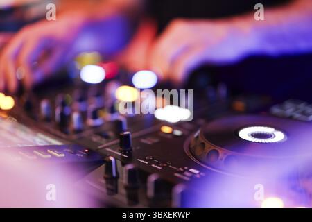 Hände eines DJ an der Steuerung eines bunt beleuchteten Mischpults, DJ ...