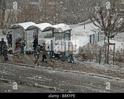 Fallender Schnee von Kindern an der Bushaltestelle in die Stadt ...
