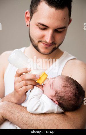 Der Vater füttert das Neugeborene mit Milch in einer Plastikflasche ...