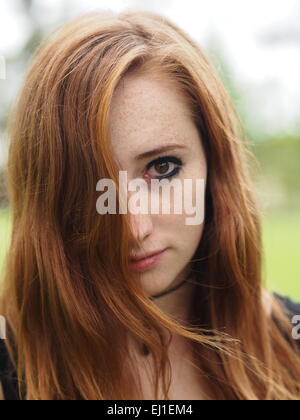 Ein Mädchen mit langen roten Haaren und Sommersprossen steht neben dem Baum im Sommerpark ...