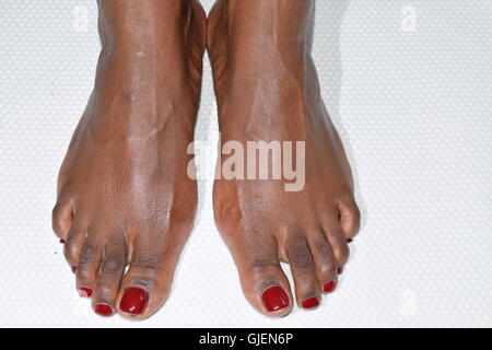 Schwarze Frau die Füße frisch lackiert und überquert auf einem weißen ...