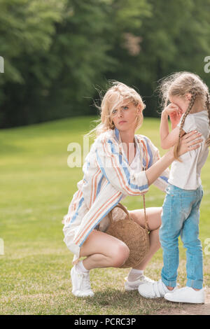 Junge Mutter umarmt ihre weinende kleine Tochter. Traurige Tochter in den Armen ihrer Mutter ...