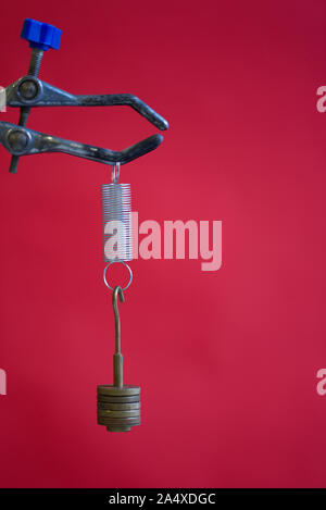 Masses accrochée à un ressort étiré isolé sur un fond rouge. Expérience ...