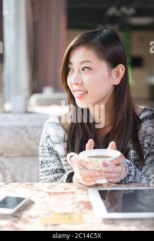 Portrait d'une jeune fille moderne assis avec un café dans un café, souriant tout en regardant ...