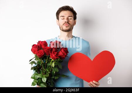 Petit ami romantique en attente de baiser, tenant bouquet de fleurs de roses et grand coeur ...