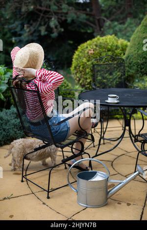 Une jeune fille gaie est assise dans l'herbe verte épaisse et fait un geste de main avec un ...