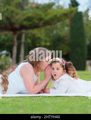 Mère chuchote tentement dans l'oreille de sa fille heureuse dehors ...