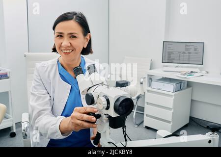 Portrait de gynécologue assis près d'une chaise gynécologique et d'une machine à ultrasons dans ...