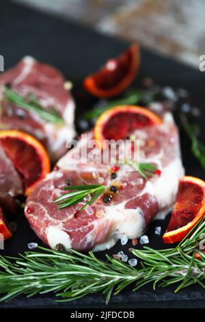 Steaks de porc crus marinés au romarin et à l'orange sur un panneau de ...