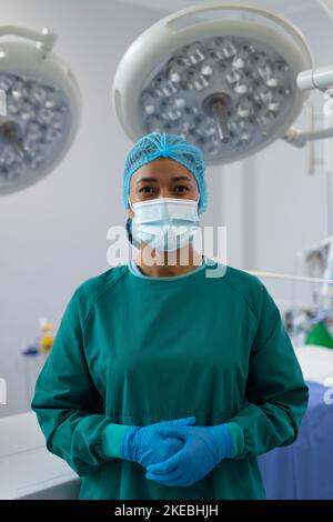 Portrait de la femme chirurgien biracial dans le masque chirurgical, le ...