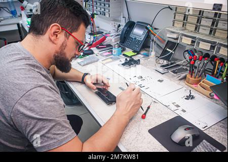 Atelier de réparation électronique, un réparateur est entouré d'outils ...