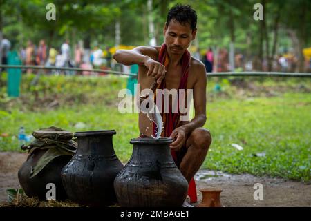 An Indian Rabha tribal Hindu priest serves traditional rice beer to the ...
