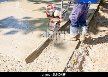 Le travailleur de la construction porte des gants pour niveler le béton ...