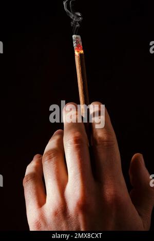 La main d'un homme tient une cigarette allumée sur un fond sombre ...