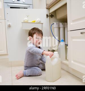 Un enfant joue avec des produits chimiques de nettoyage sous l'évier ...