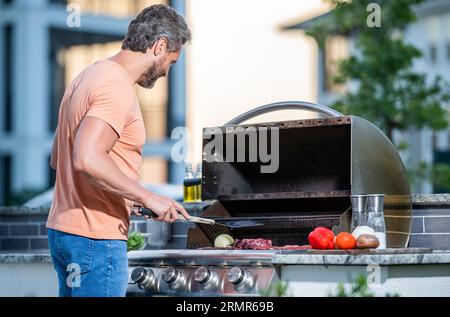 Homme grillant des steaks à la perfection sur un barbecue fumé ...