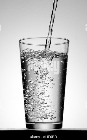 L'eau étant versée dans le verre sur fond blanc, rouge dans le fond du ...