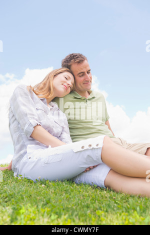 Couple aimant assis sur l'herbe dans le parc embrasse passionnément sur ...