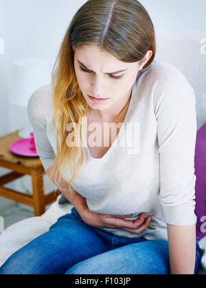 Des douleurs abdominales. 20-year-old woman holding her abdomen ...