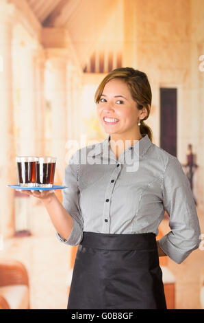 Jeune brunette serveuse en uniforme avec sourire amical, holding up bac ...
