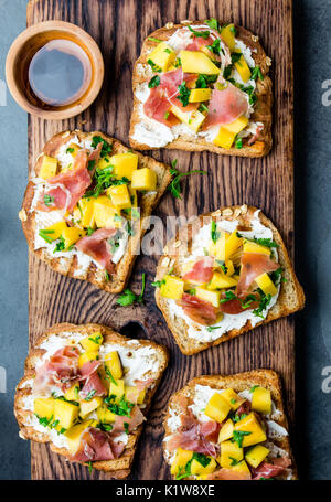 Toasts avec du fromage à la crème, jambon jamon serrano et mangue servi ...