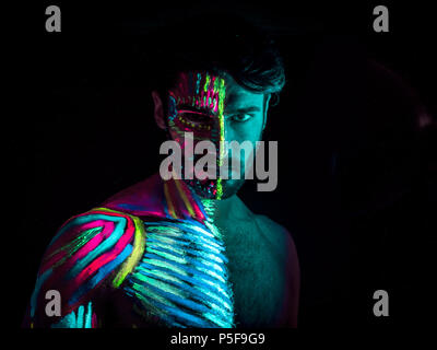 Jeune homme peint à la peinture fluorescente sur le visage et le torse ...