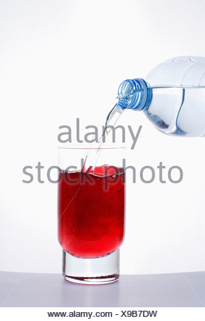 Verser de l'eau dans un verre de sirop de grenadine Photo Stock - Alamy