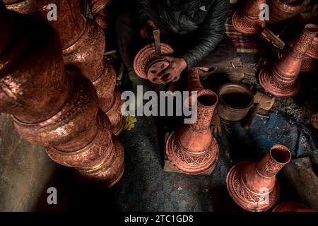 Un fabbro Kashmiri lavora su una ciotola di rame in un laboratorio. L ...