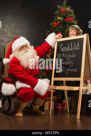 Babbo Natale seduto vicino a lavagna con wishlist segno e la copia in ...